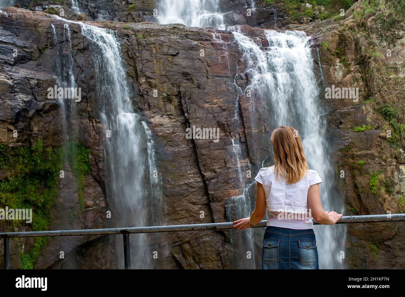 A girl stands in front of a waterfall and admires the beautiful view of ...