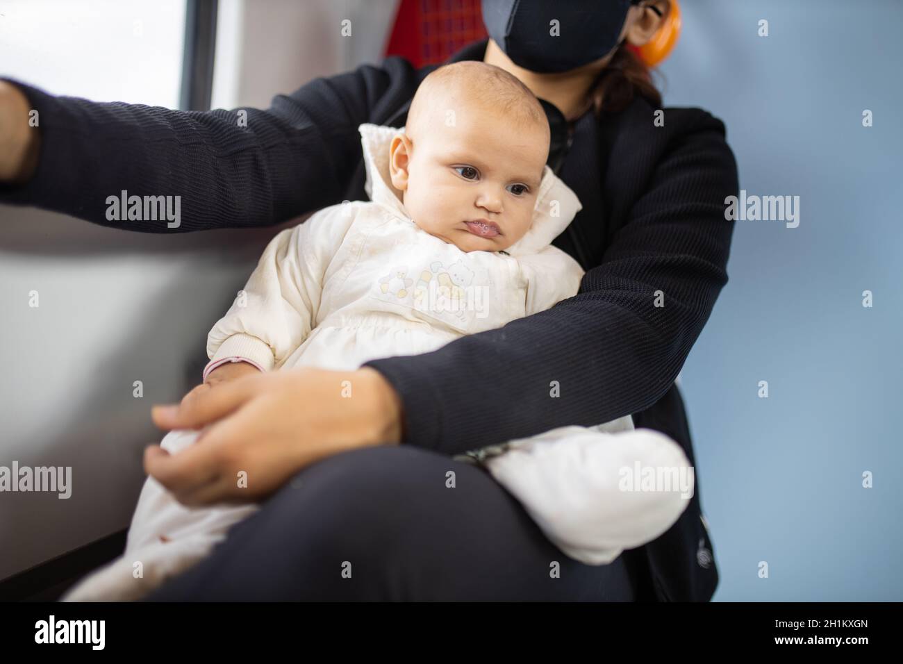 Distracted-looking baby in white clothing resting on the legs of her ...