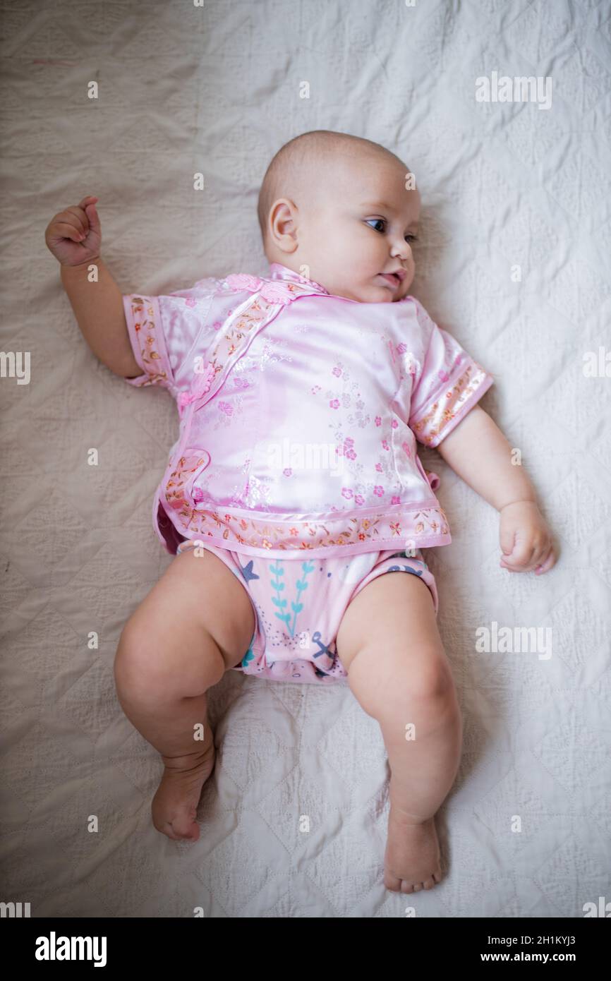 Distracted adorable baby girl from above in Asian pink attire lying ...