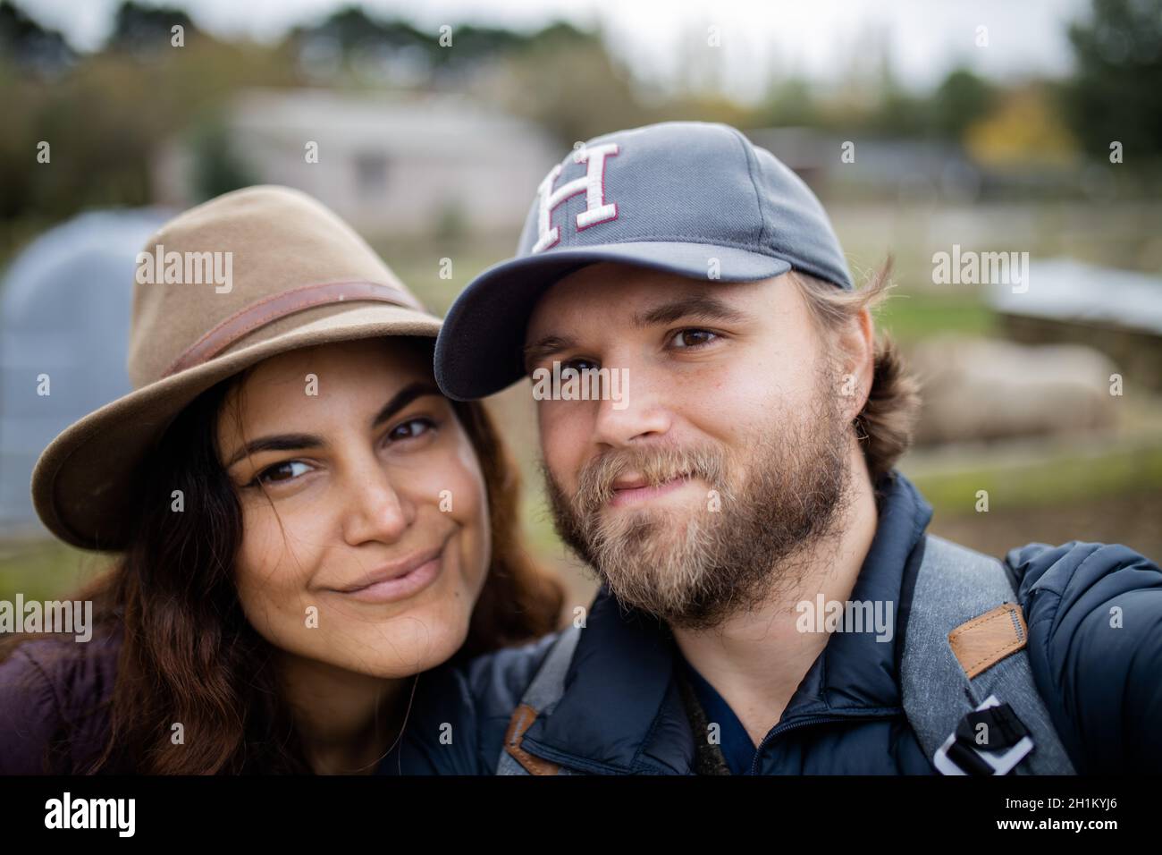 Portrait of happy hatted wife and husband smiling with blurry farm as ...