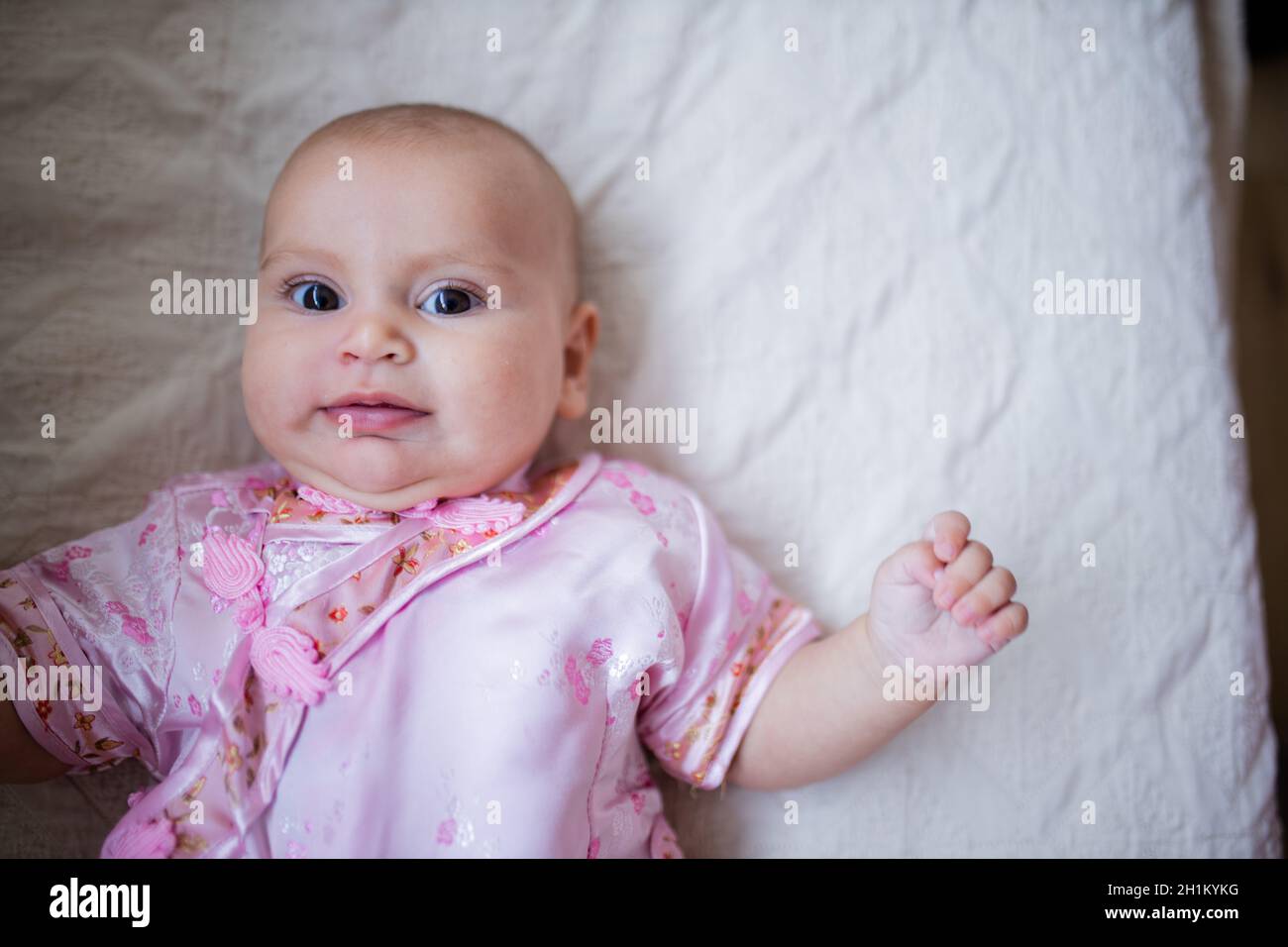 Curious adorable baby girl from above in Asian pink attire lying down ...
