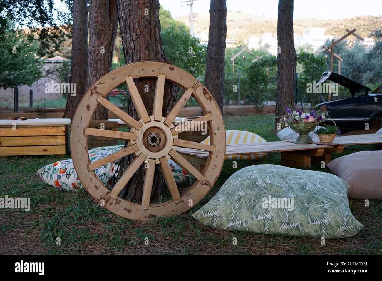 View of a big wooden wheel of a cart in the garden, pillows and tree ...