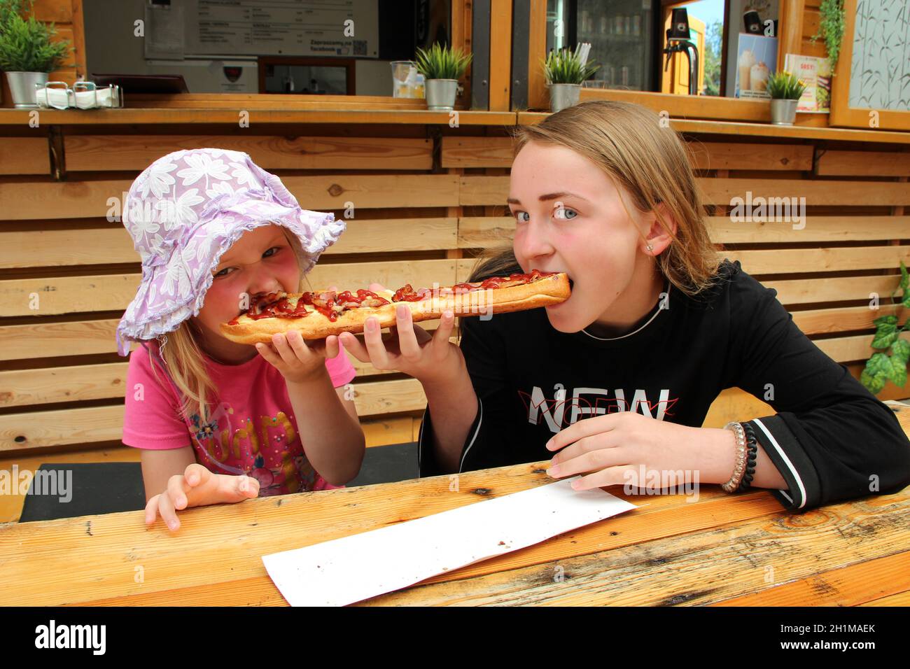Two girls eat one big sandwich at at the same time. Two sisters eat a ...