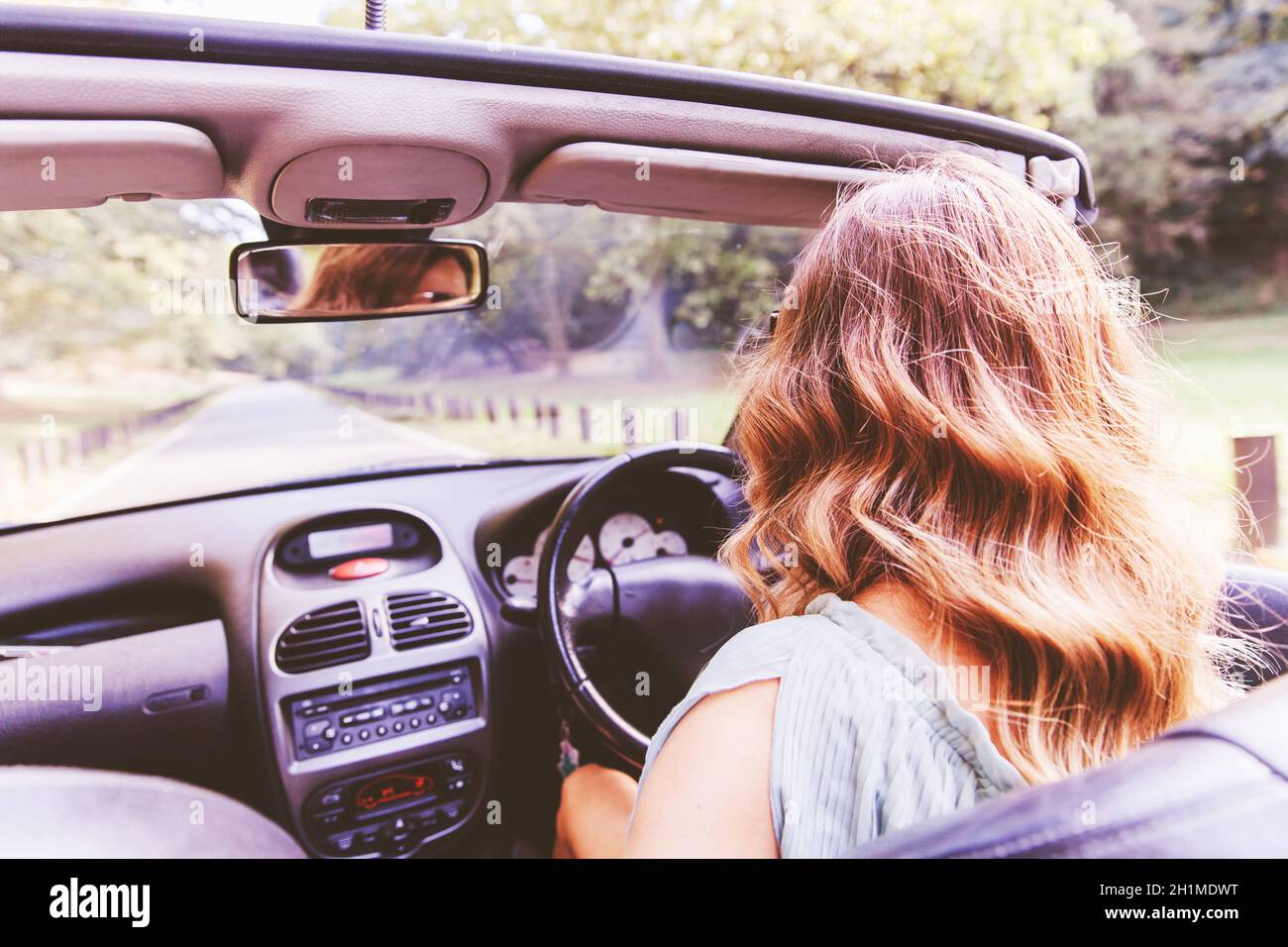 Pretty young woman driving convertible car on summer day. Wearing ...