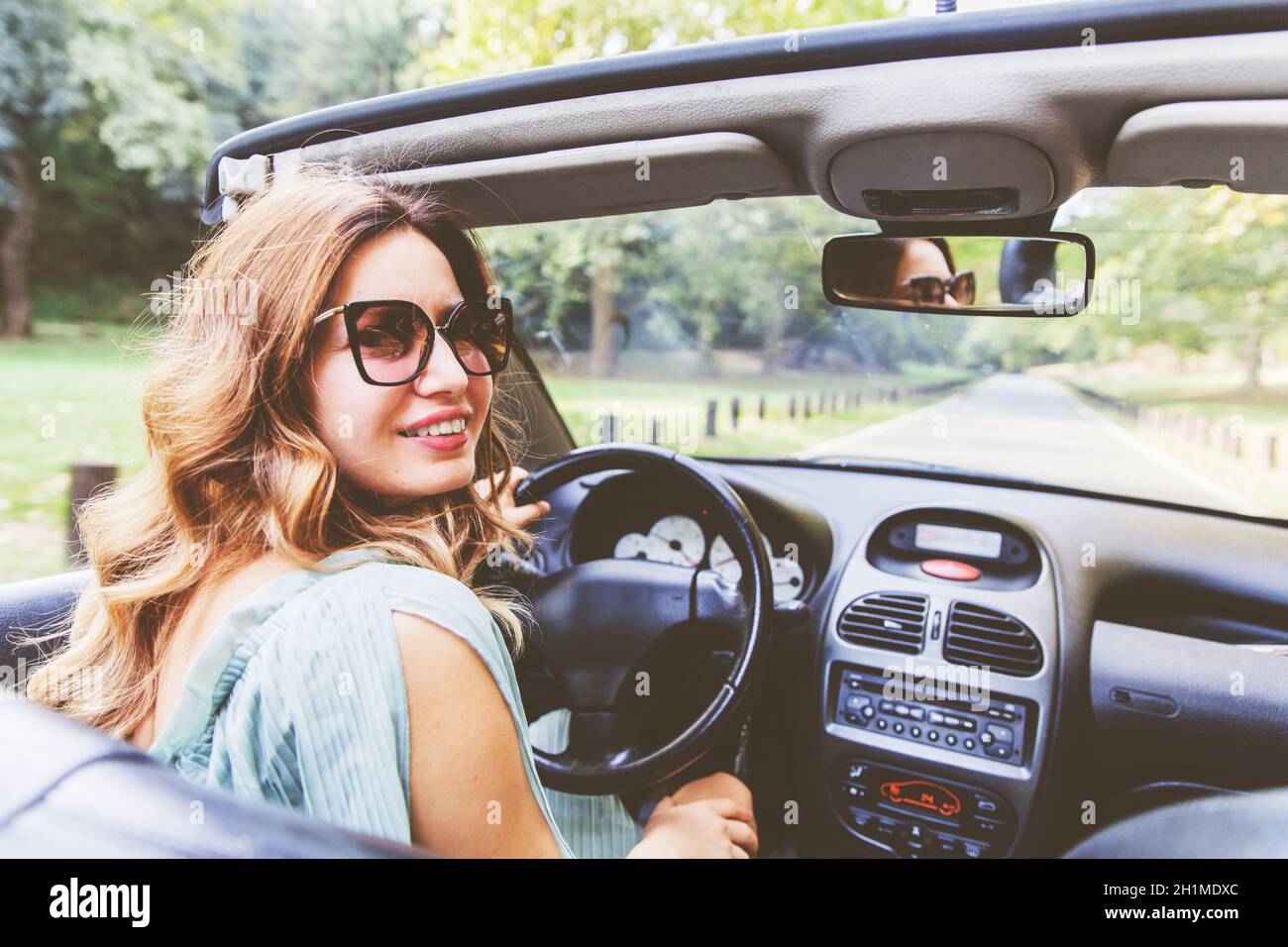 Pretty young woman driving convertible car. Happy girl drive on summer ...