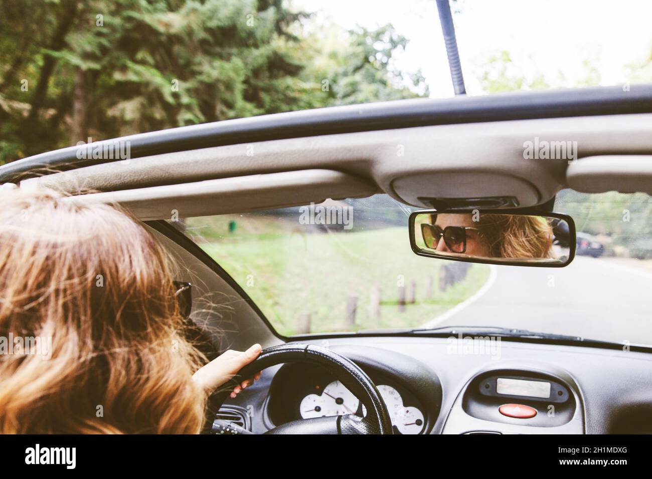 Pretty young woman driving convertible car on summer day. Wearing ...