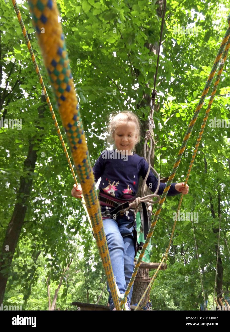 The girl climbing in adventure rope park against green trees Stock ...
