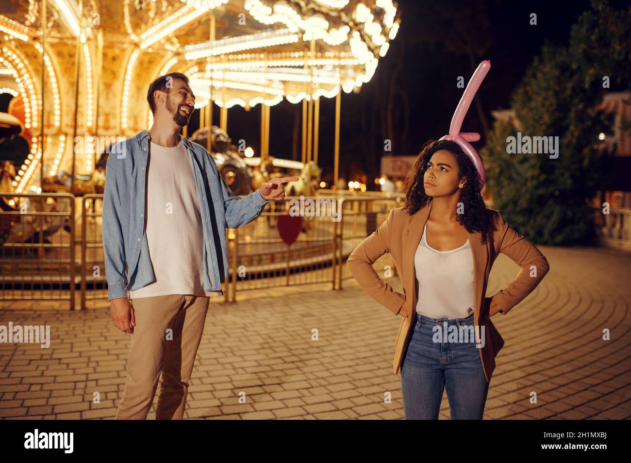 Funny love couple joking in night amusement park. Man and woman relax ...