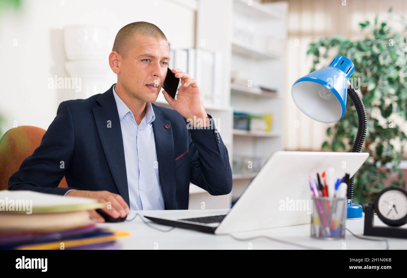 Focused office employee talking on mobile phone at workplace Stock ...