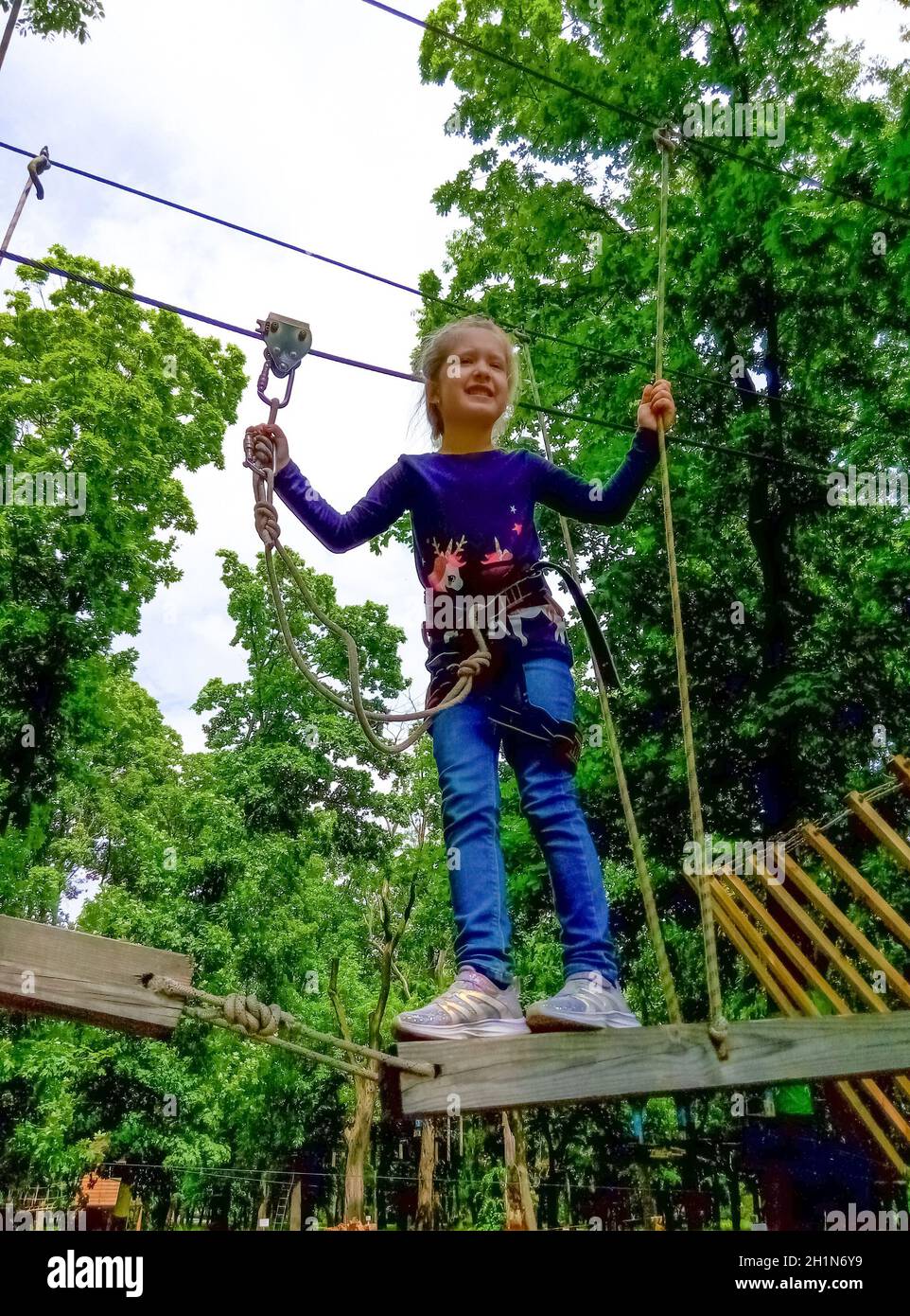The girl climbing in adventure rope park against green trees Stock ...