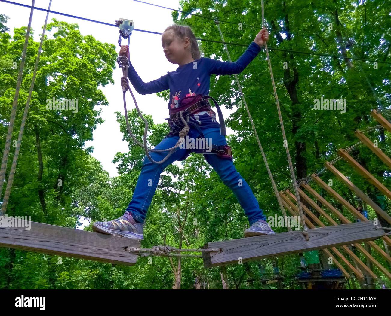 The girl climbing in adventure rope park against green trees Stock ...