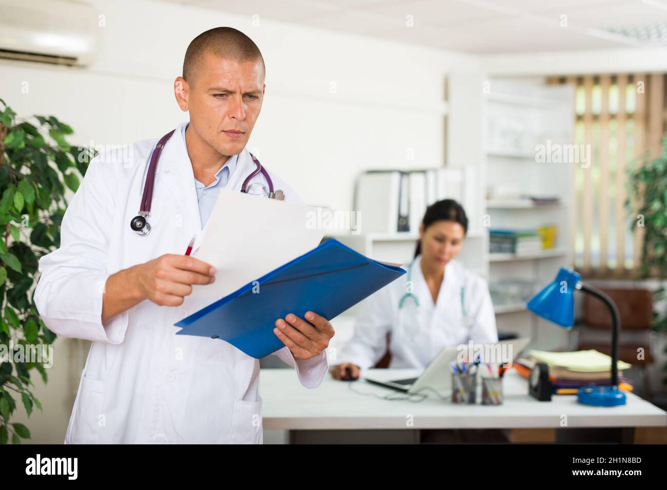 Doctor standing in modern office with document Stock Photo - Alamy