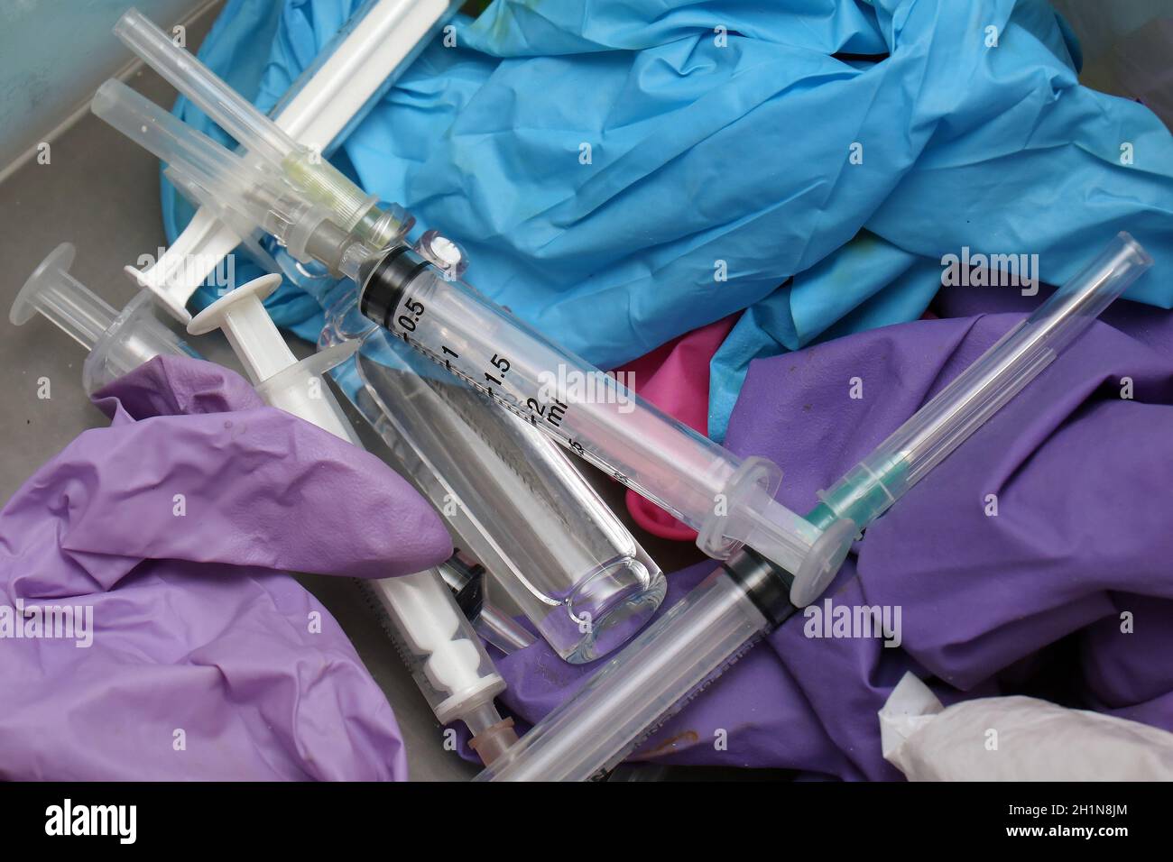 Large pile of used medical syringes with needles on colorful gloves ...