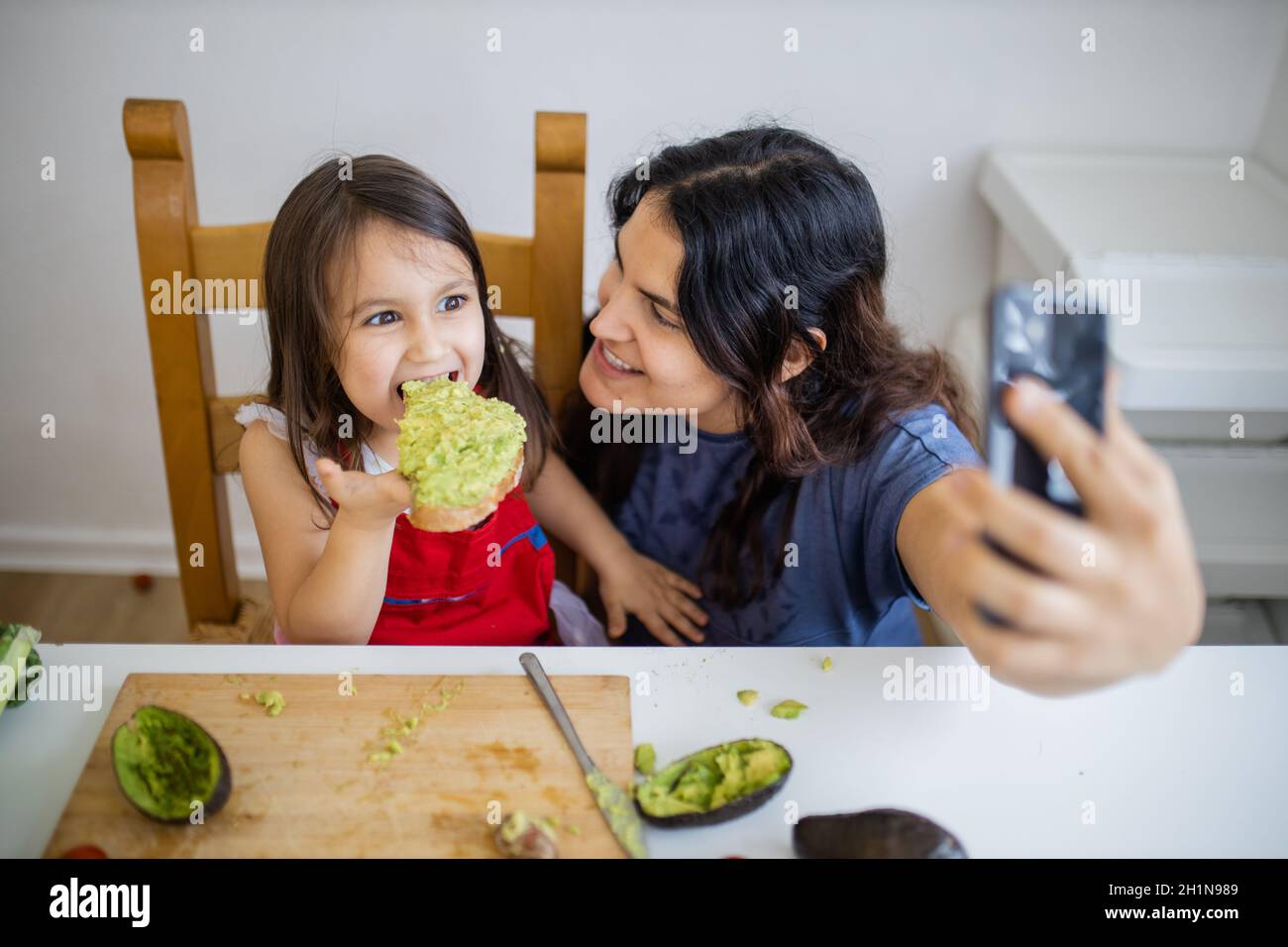 Happy mother and daughter taking selfie while eating toast with avocado ...
