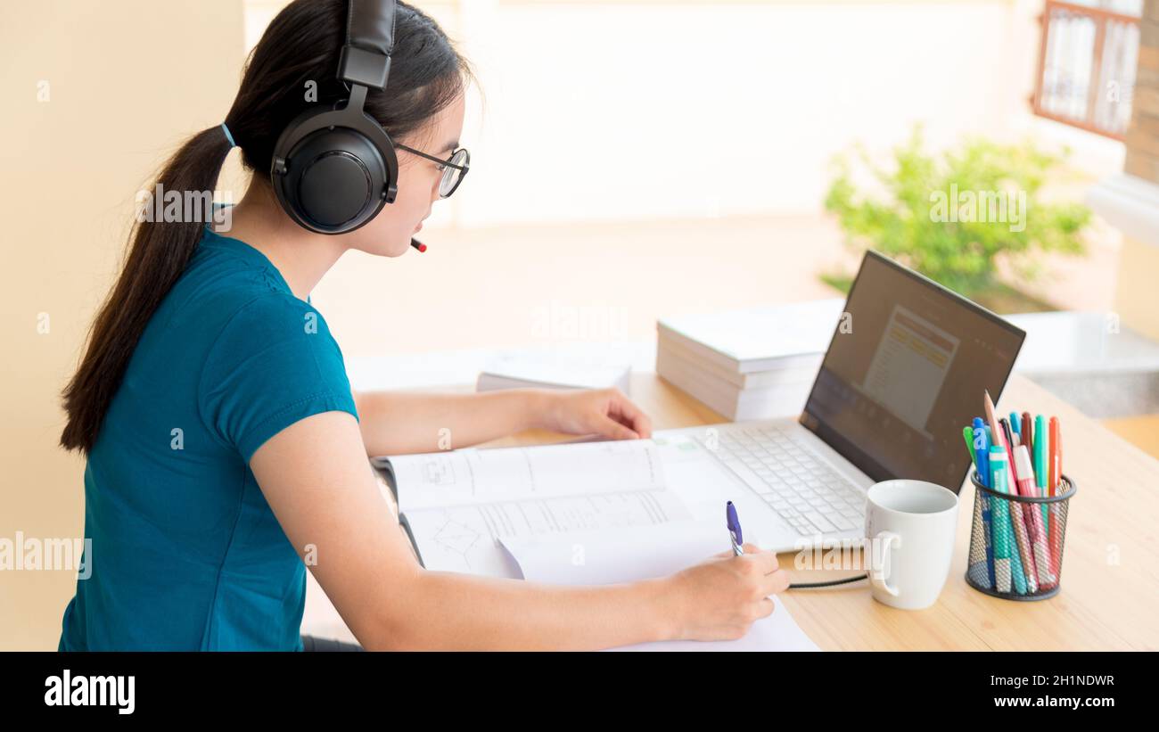 Asian teenage girl student with a headset looking at the laptop screen ...