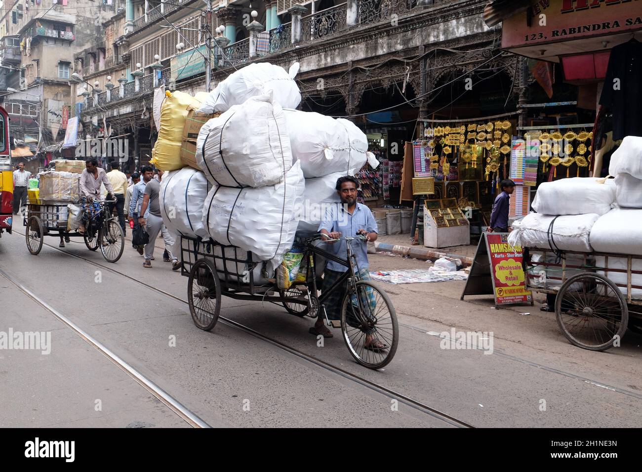 Worker pulling bale on tricycle rickshaw along a busy street in Kolkata ...