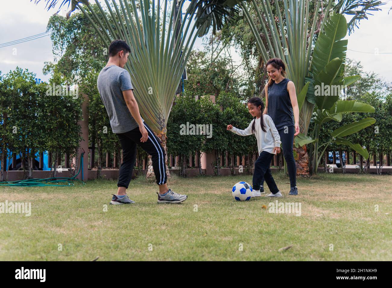 Asian young mother, father and child daughter playing soccer outside in ...