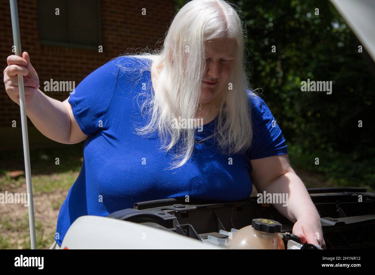 Blind woman checking under the hood of an automobile near the coolant ...