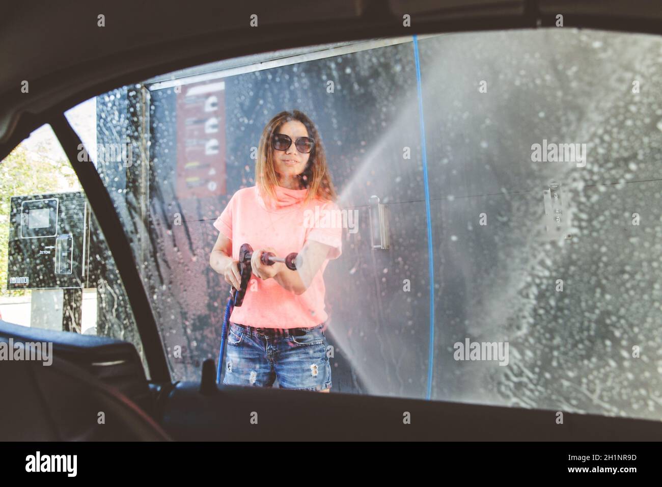 Woman washing her car with high pressure sprayer at self-serve car wash ...