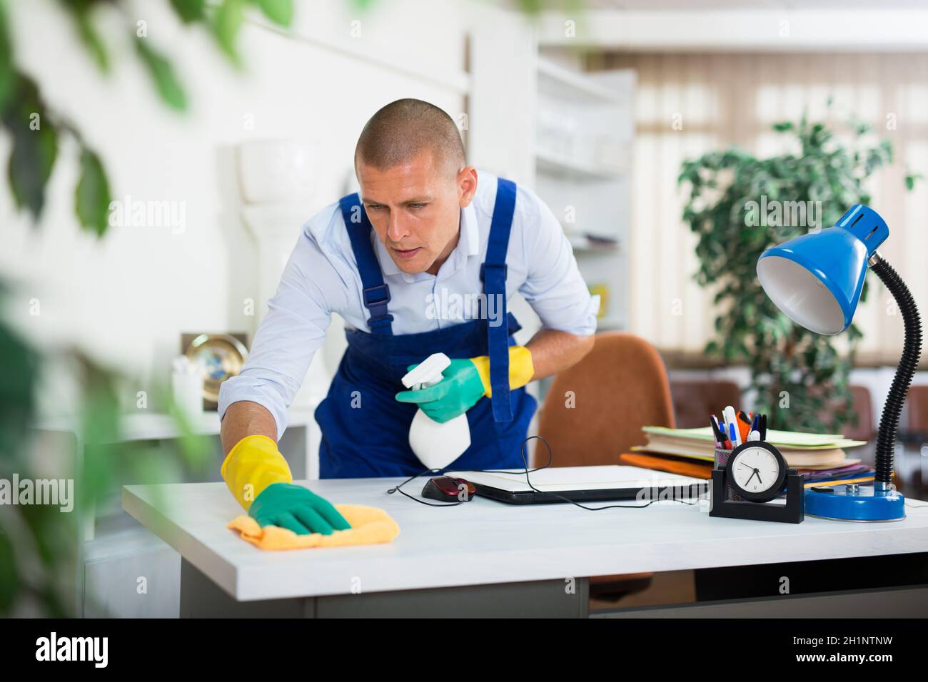 Man in uniform is cleaning dust from the desk in office Stock Photo - Alamy