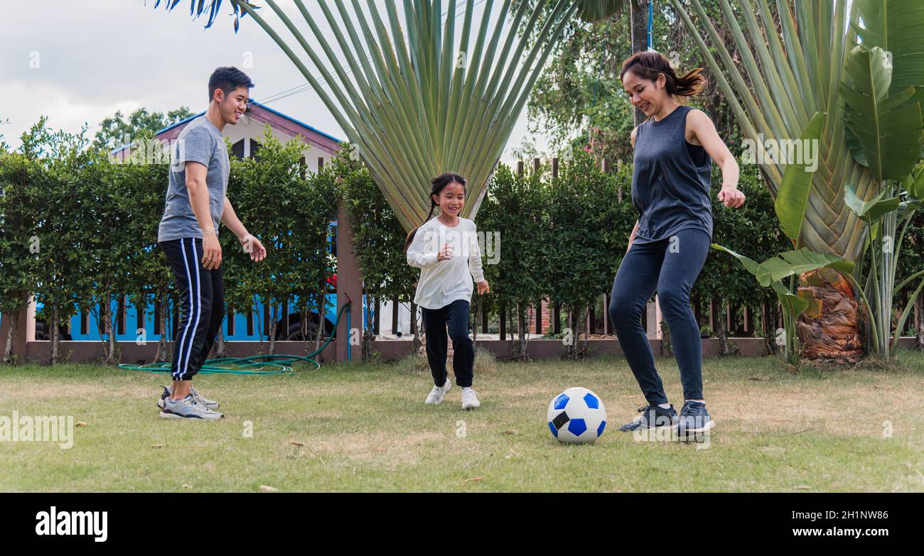 Asian young mother, father and child daughter playing soccer outside in ...