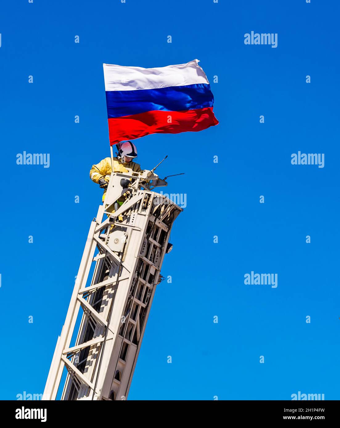 A firefighter secures a Russian flag on the fire ladder on background ...