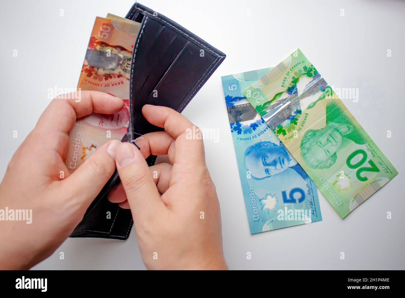 A person opening a wallet and spending canadian dollars on a white ...