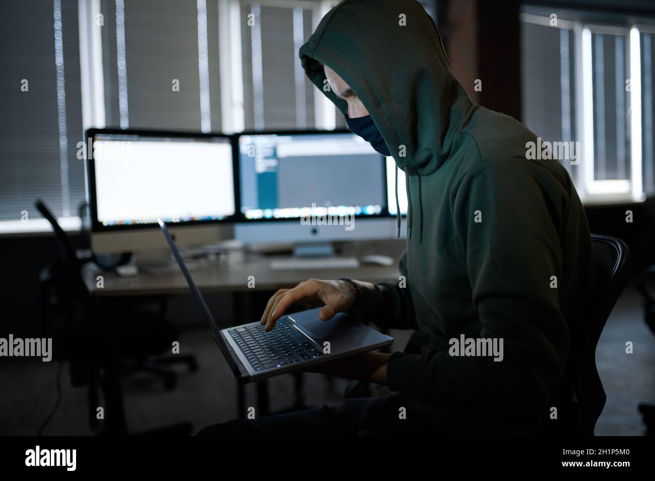 Male internet hacker in hood holds laptop, front view. Illegal web ...