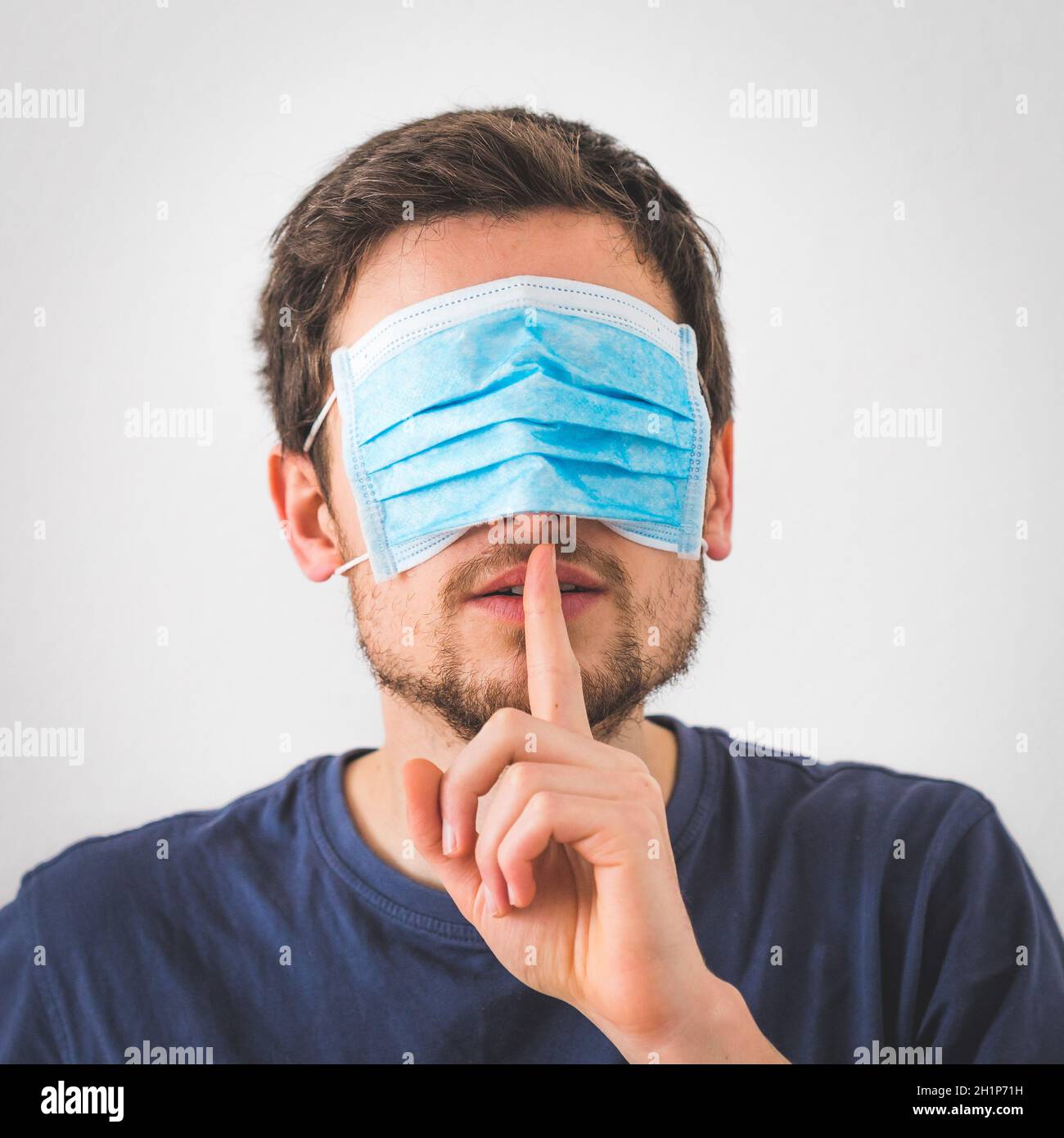 Young angry man with face mask over the eyes is doing a psst! gesture ...