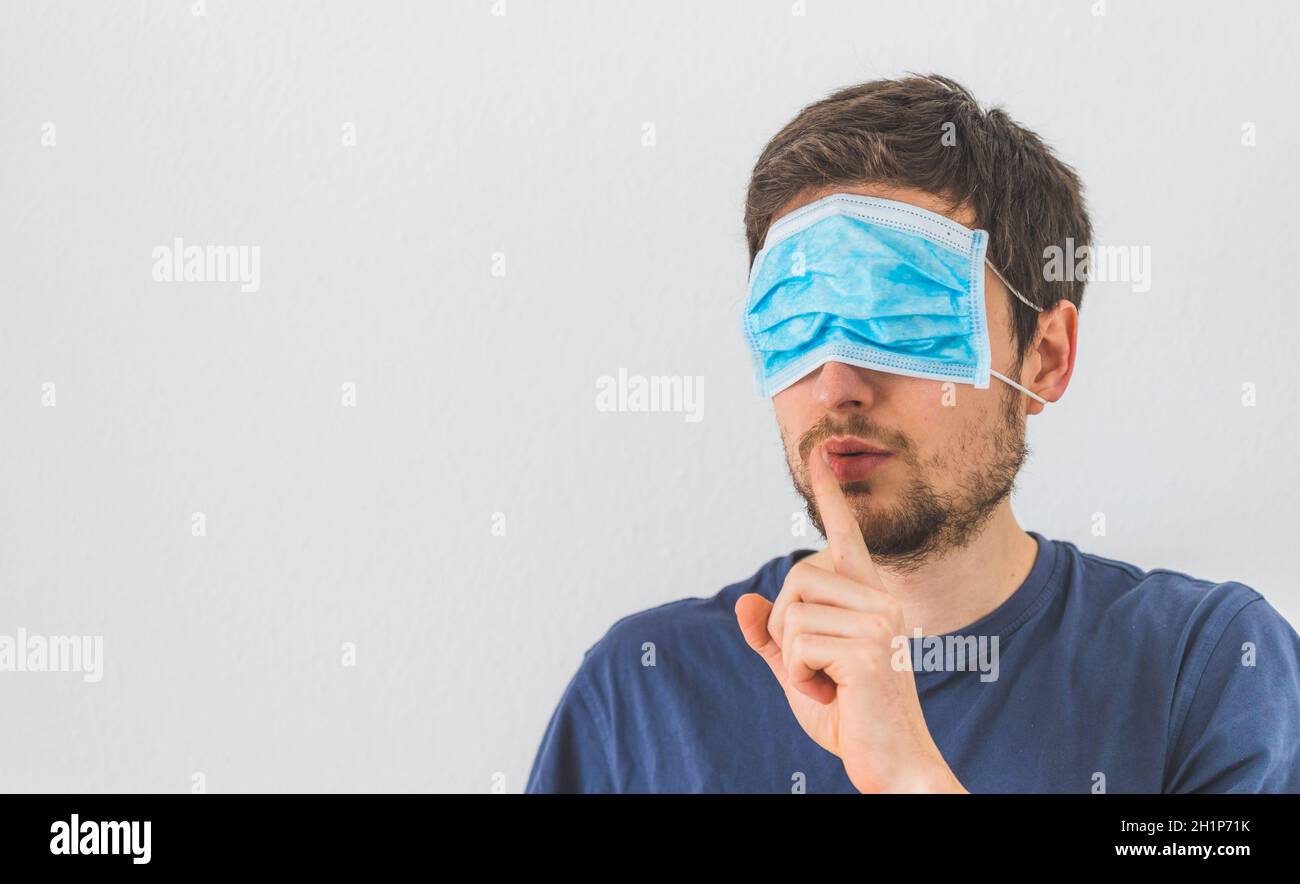 Young angry man with face mask over the eyes is doing a psst! gesture ...