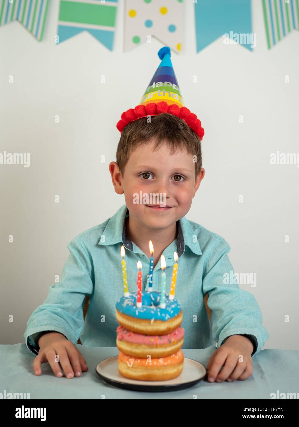 Five year old boy in his birthday and festie donuts cake with candles ...