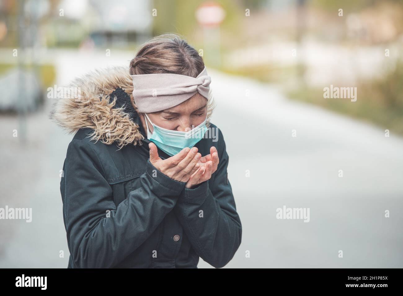 Young sneezing woman outdoors wearing a face mask. Corona and flu ...