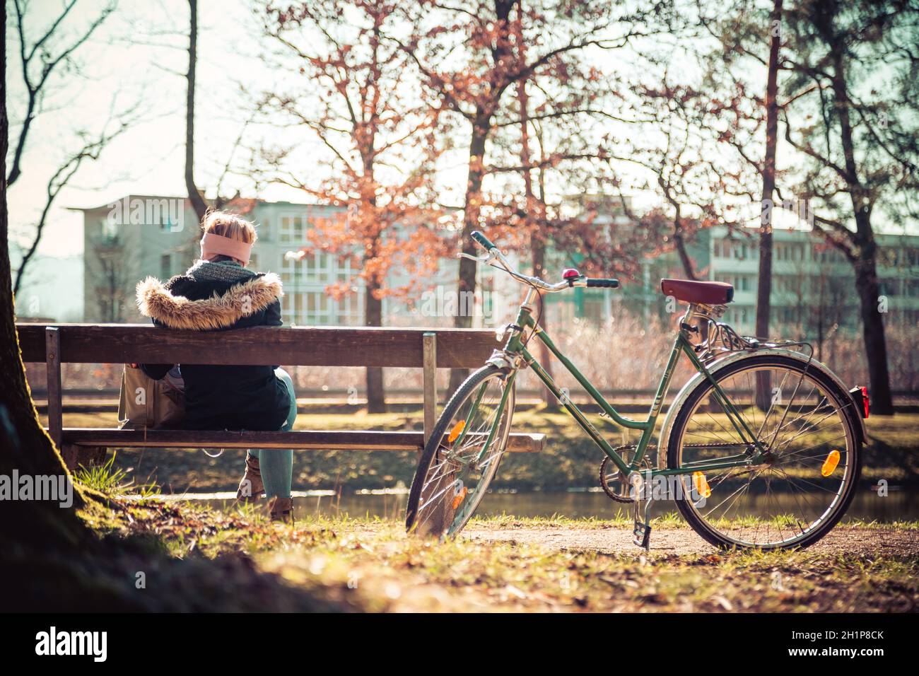 Back view of young woman with bicycle who is enjoying the sun on a park ...