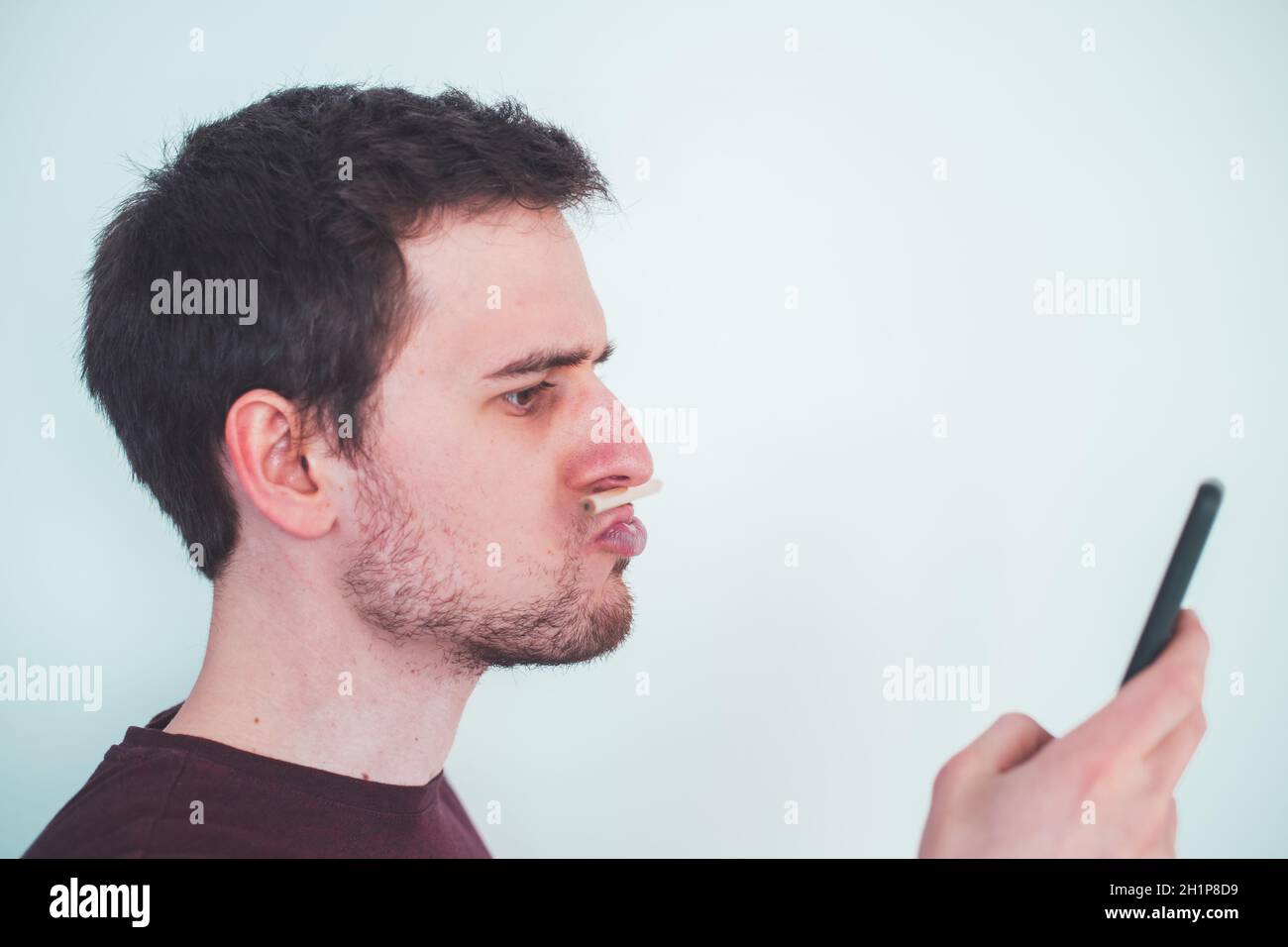 Young Caucasian man is fooling around and home, pencil trapped between ...