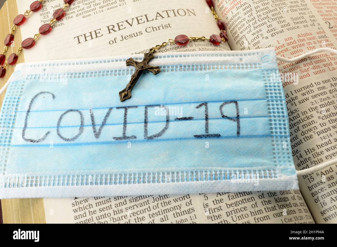 An open Bible and rosary with a mask marked with the pandemic Covid19 ...