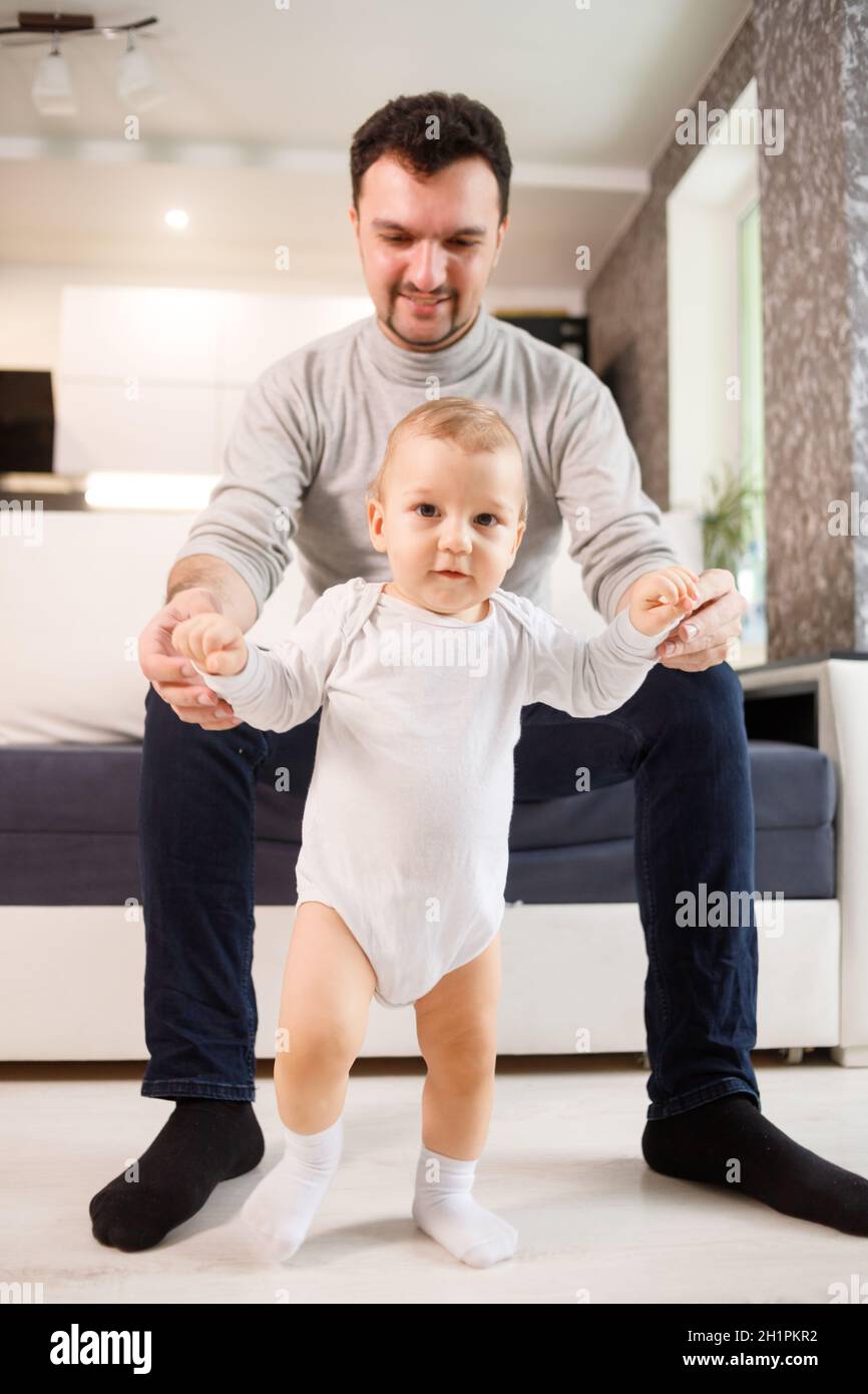 Young father assisting walking his infant son teaching to walk at home ...