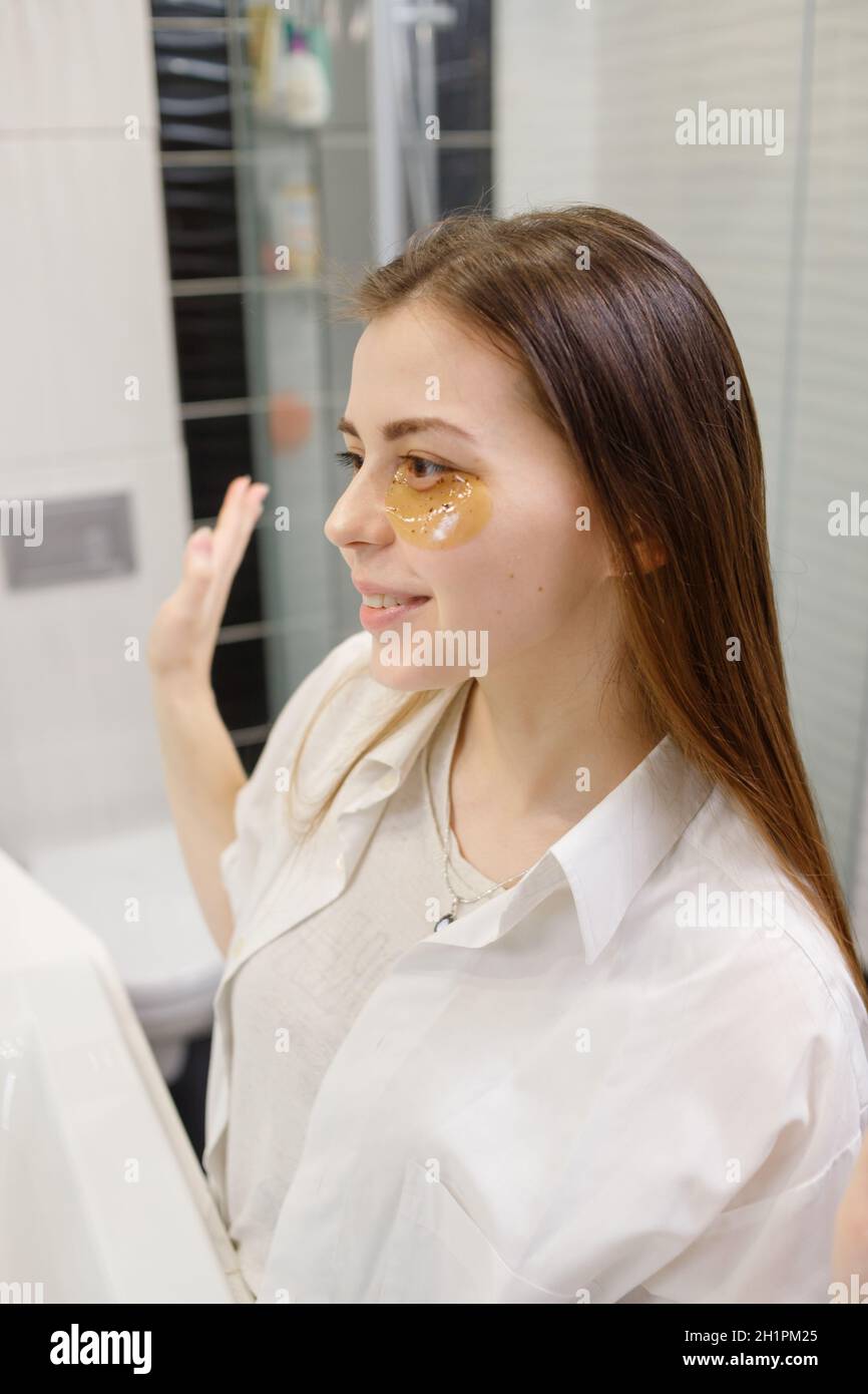 Smiling pretty woman applying hydrogel patches on under eye area ...