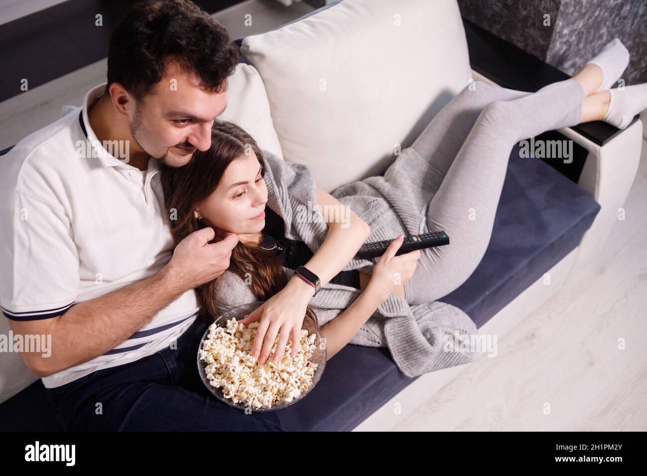 Young couple eating popcorn while watching movie lying on sofa Stock ...
