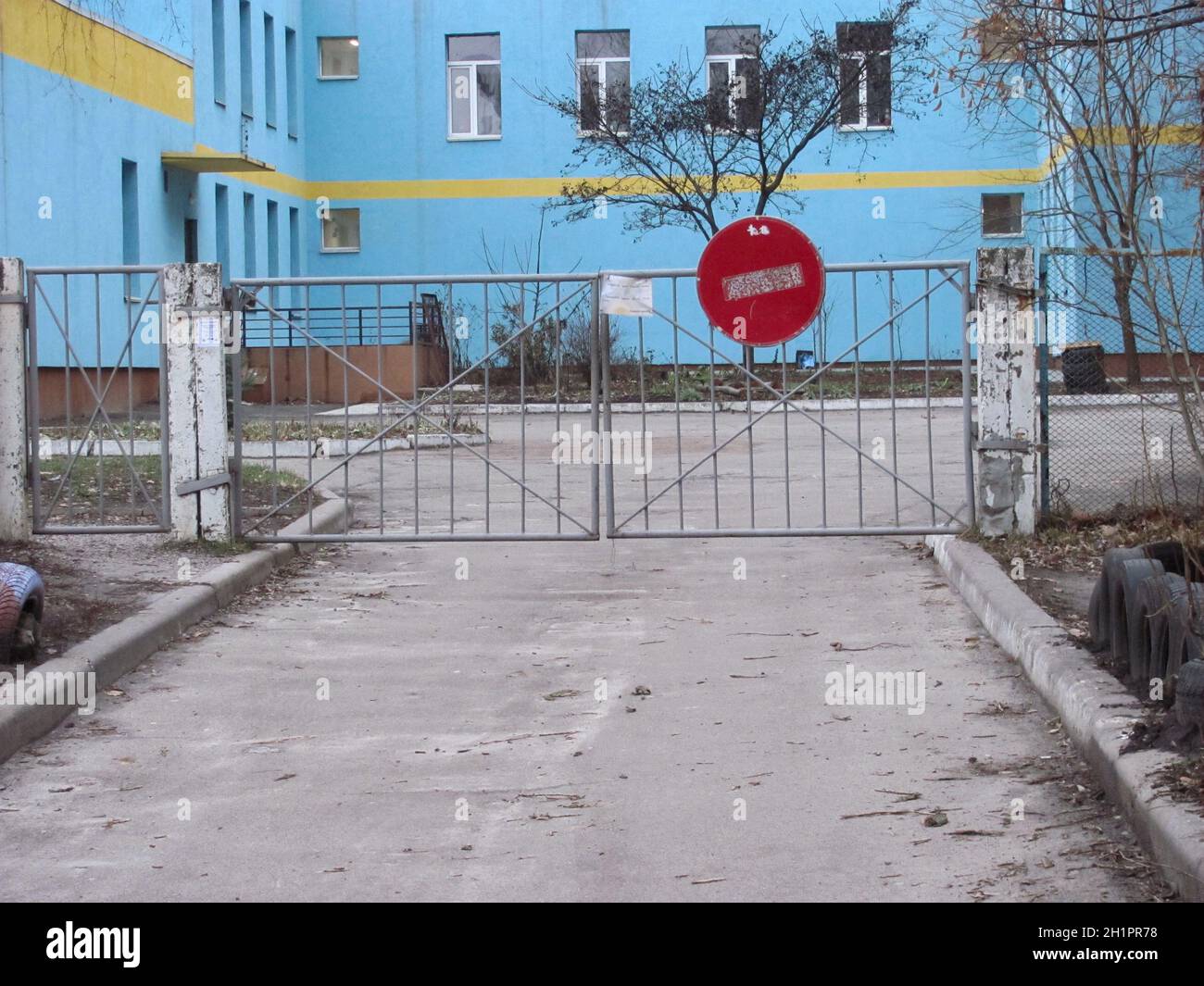 tattered gate with a no entry sign and a paper note, a blue building ...