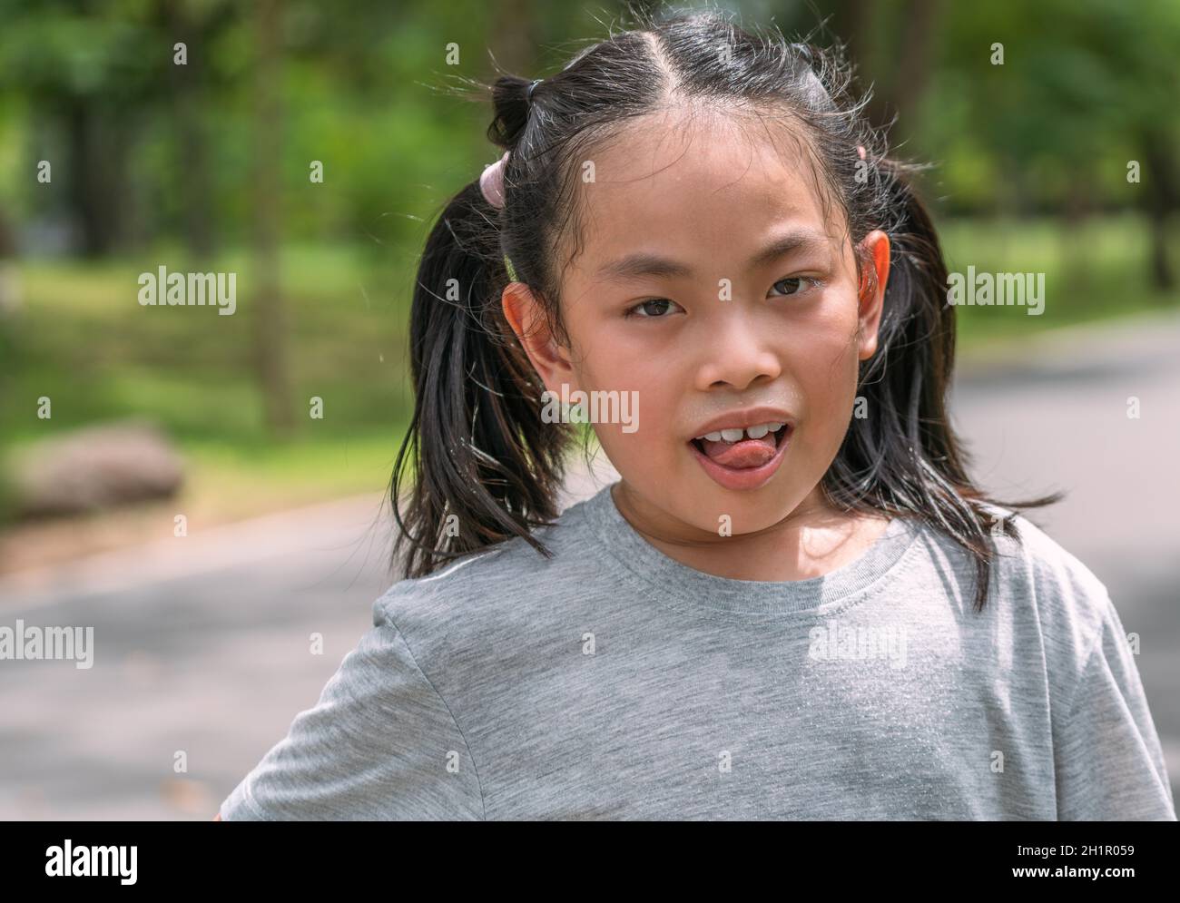 Portrait Asian child girl in the park, many sweats on the face, tongue ...