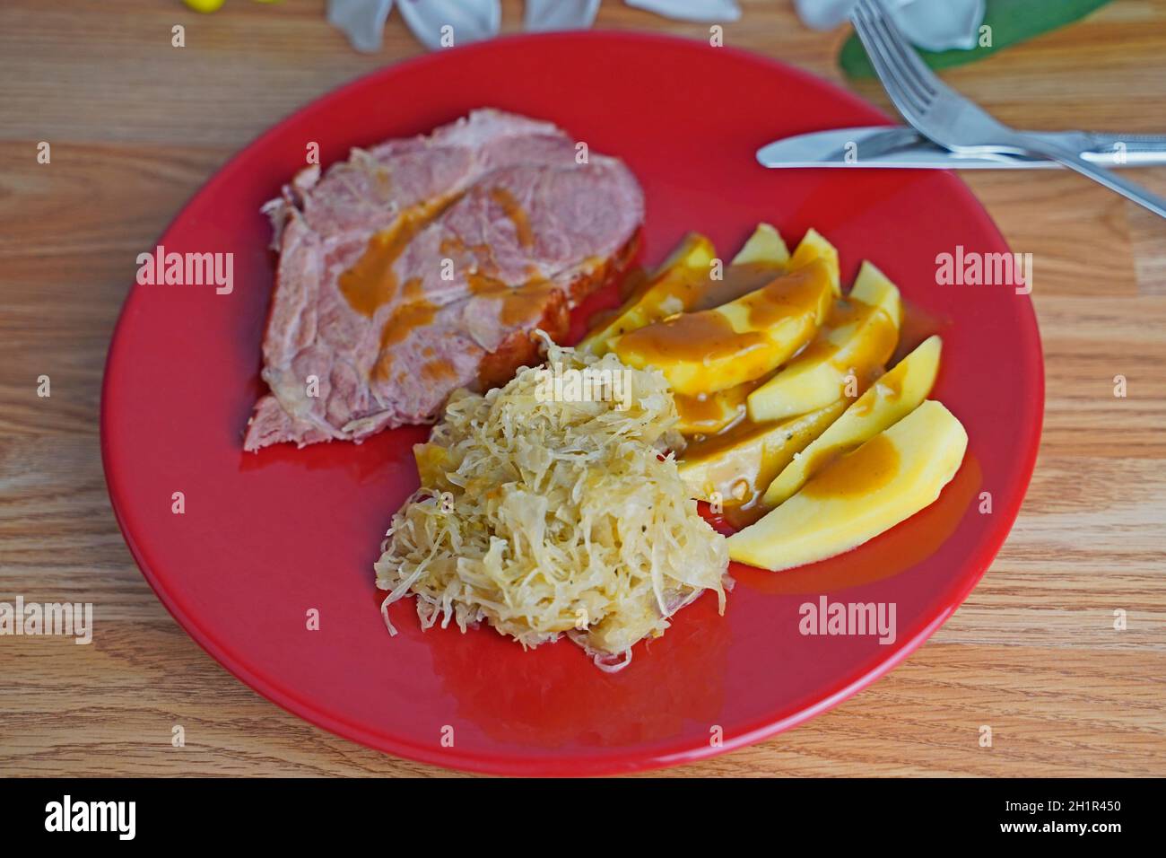 salted meat with sauerkraut and potato wedges arranged on red plate Stock Photo - Alamy