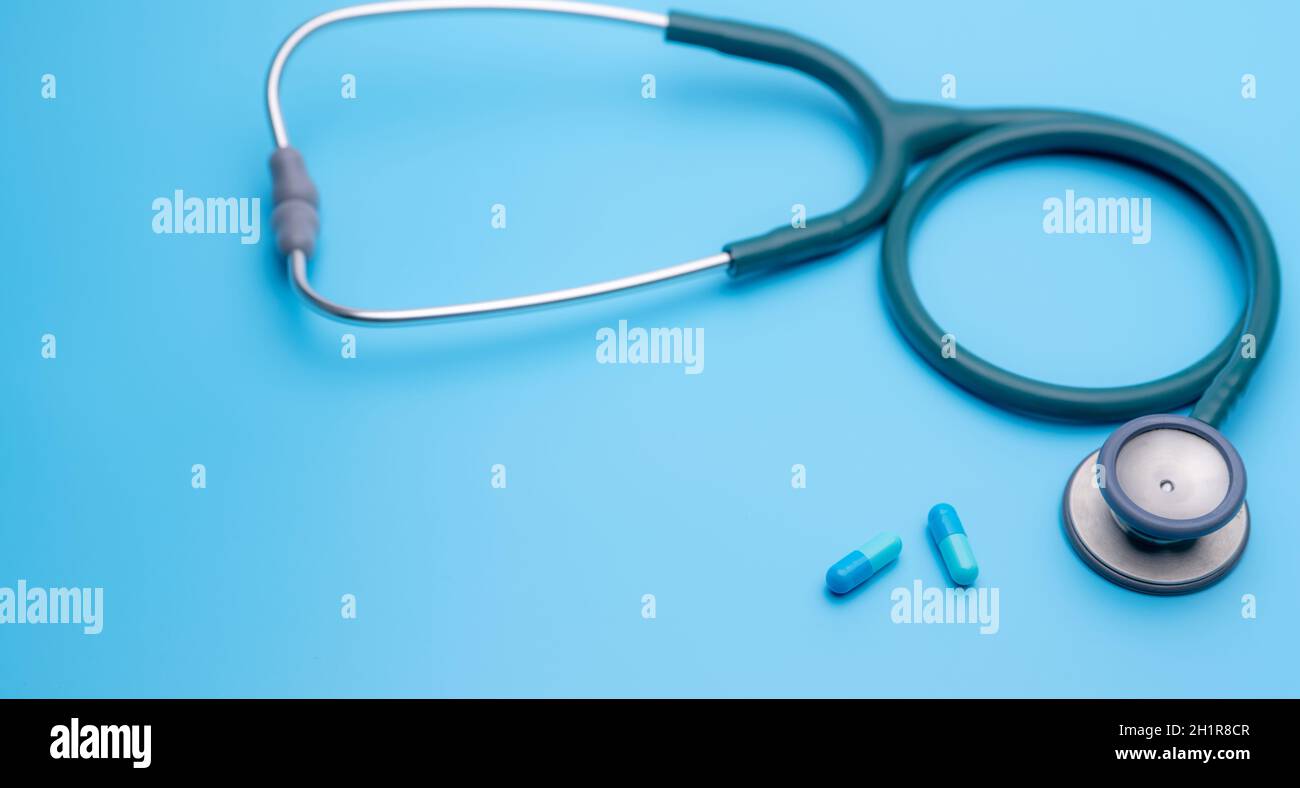Blue capsule pills and green stethoscope on blue background. Health ...