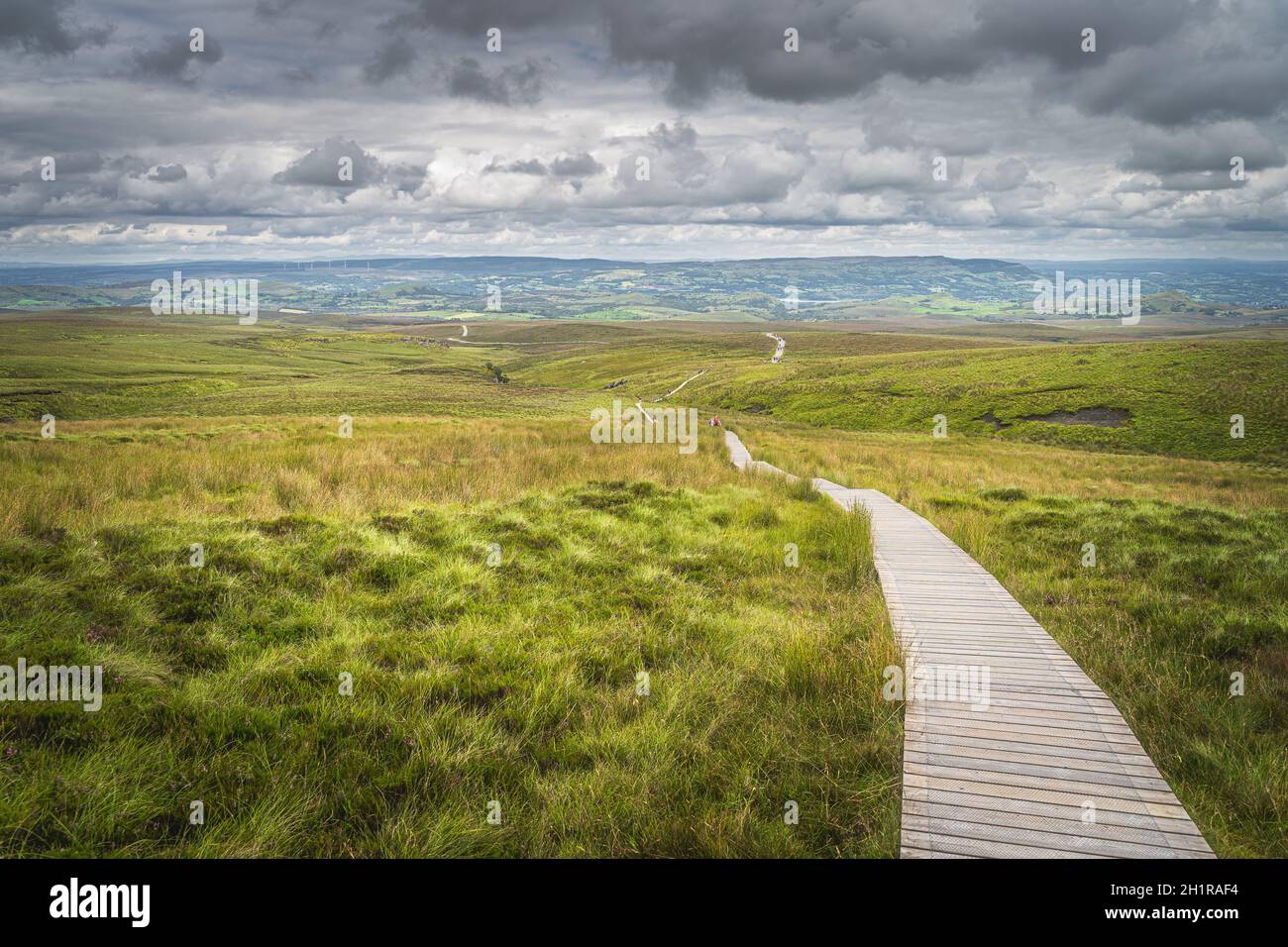 Wooden boardwalk between green hills and bog leading to distant horizon ...