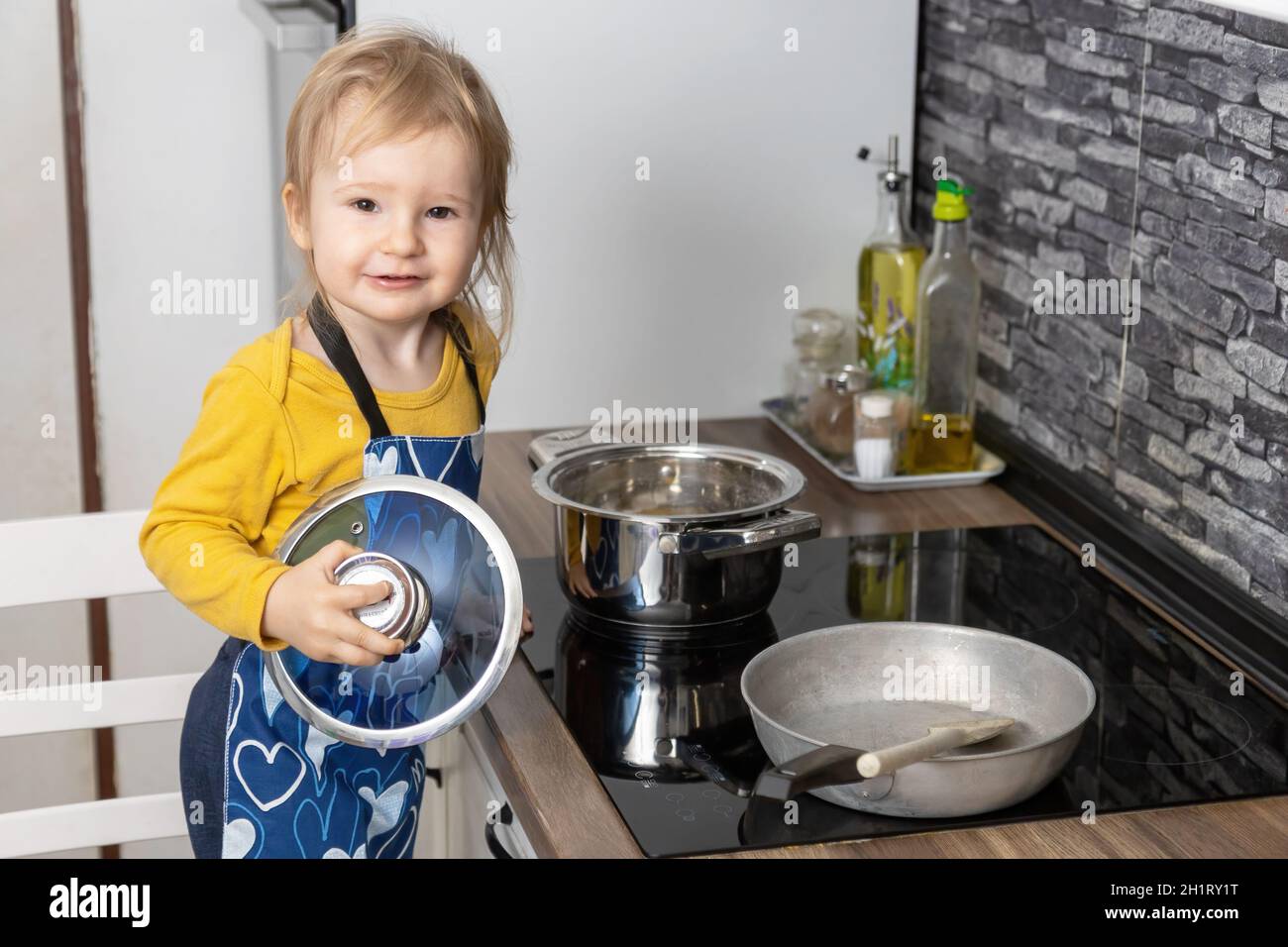 Cute little boy is posing in the kitchen holding a glass lid ...
