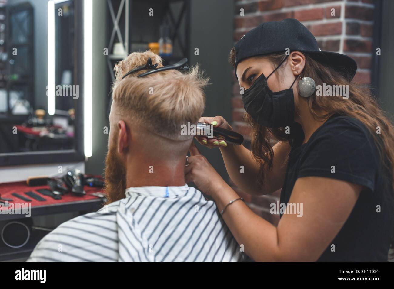 Female barber in mask cuts a man hairs with hair clipper. Hairstyle ...