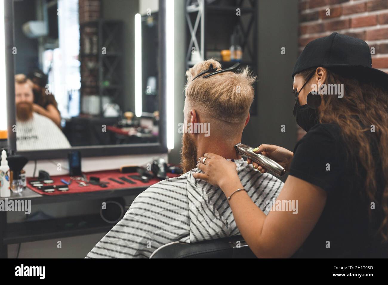 Female barber in mask cuts a man hairs with hair clipper. Hairstyle ...