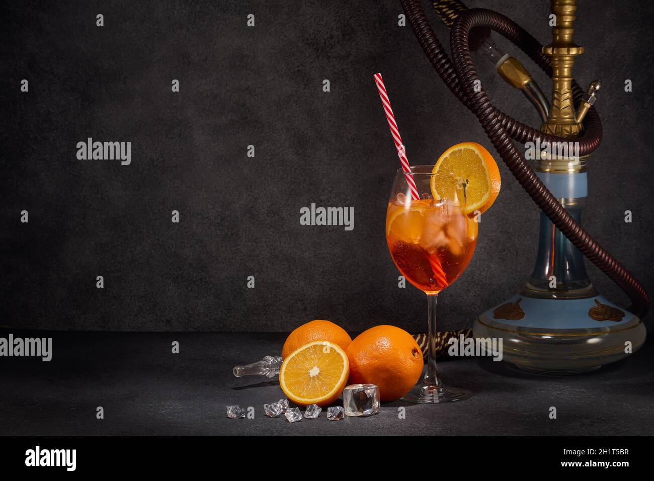 Hookah (shisha) and glass of cocktail with oranges and ice on dark grey ...