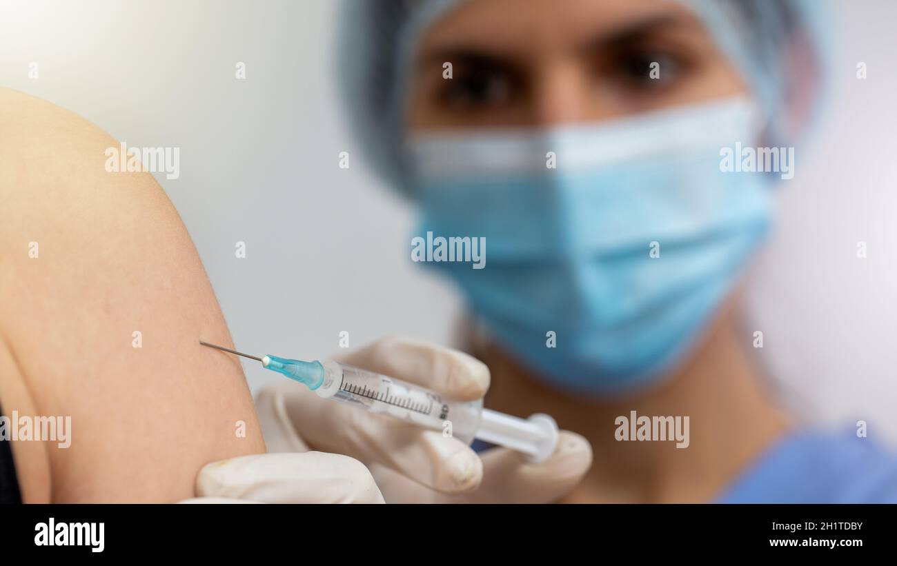 Female doctor with surgical mask giving injection to person. Nurse with ...