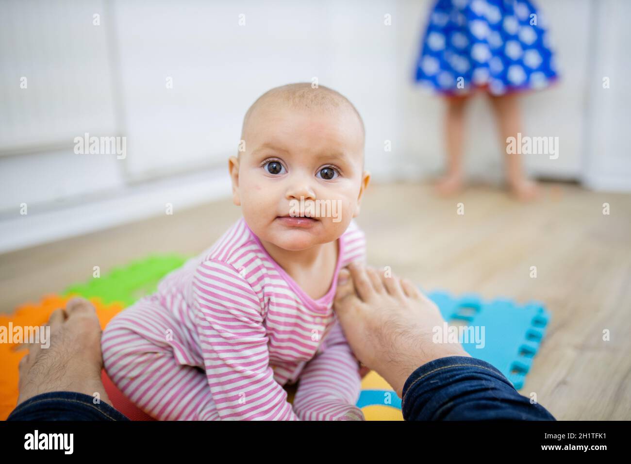 Adorable baby siting on colorful foam mat between the feet of her ...