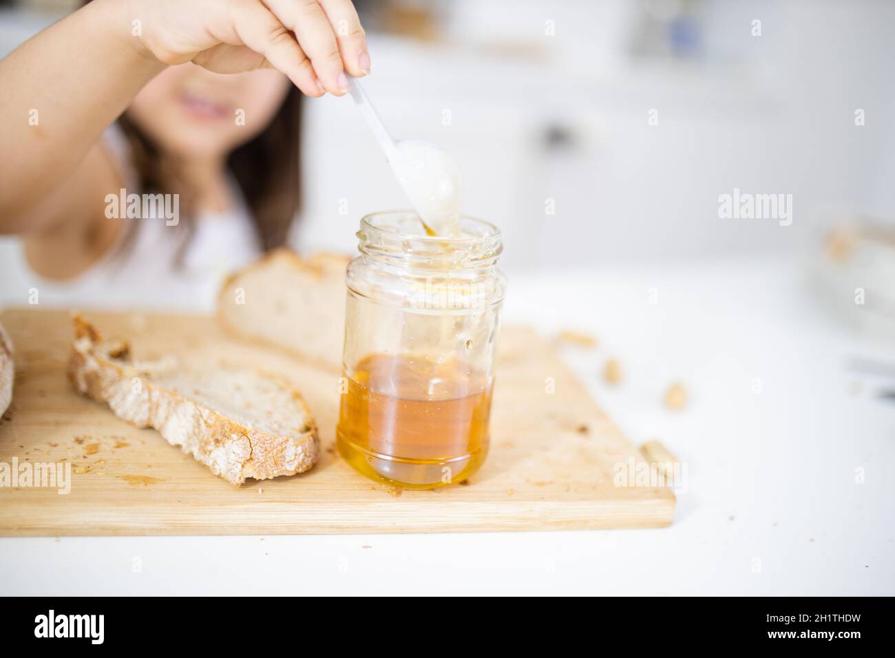 Little girl picking honey from jar next to a slice of bread above ...